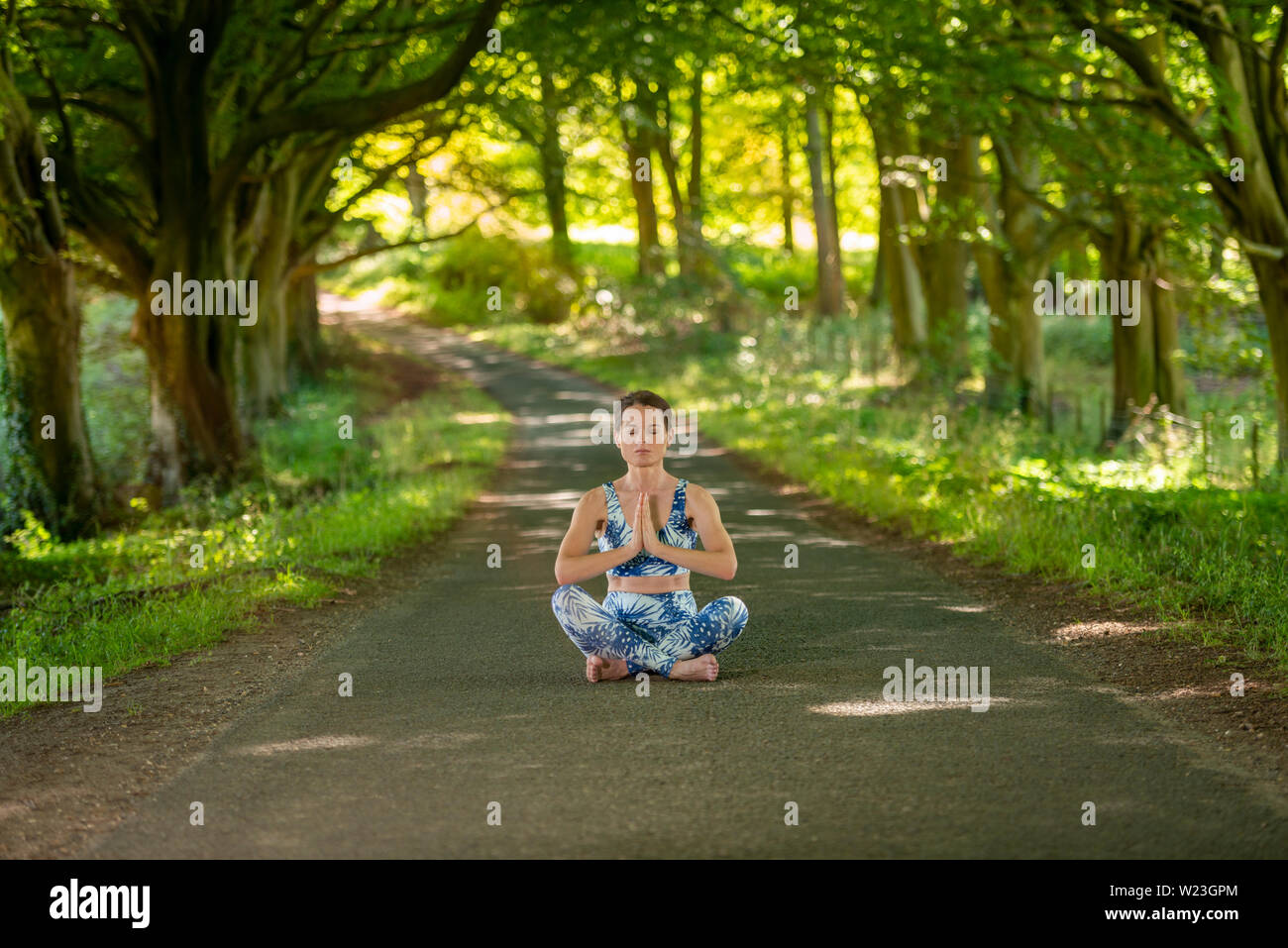 woman sitting crossed legged in the middle of a country road meditating ...