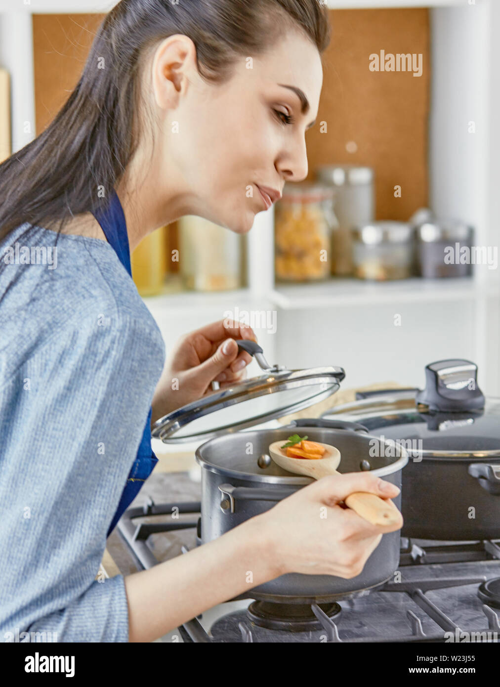 Beautiful girl is tasting food and smiling while cooking in kitchen at ...