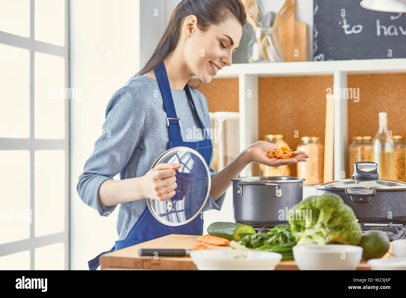 Beautiful girl is tasting food and smiling while cooking in kitchen at ...