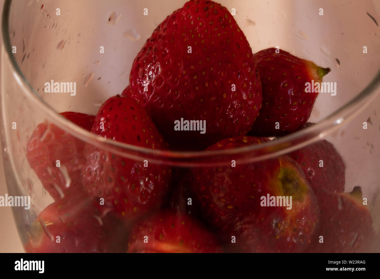 Many red strawberries inside a glass cup, taken with a white fabric ...