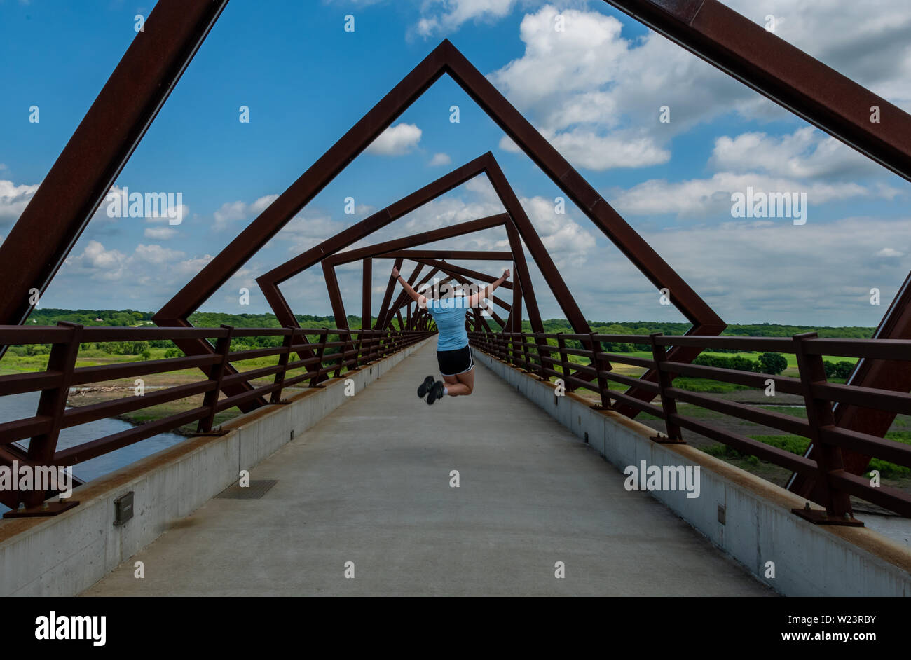 Woman Jumps Underneath Twisting Bridge Along Rails to Trail Stock Photo ...