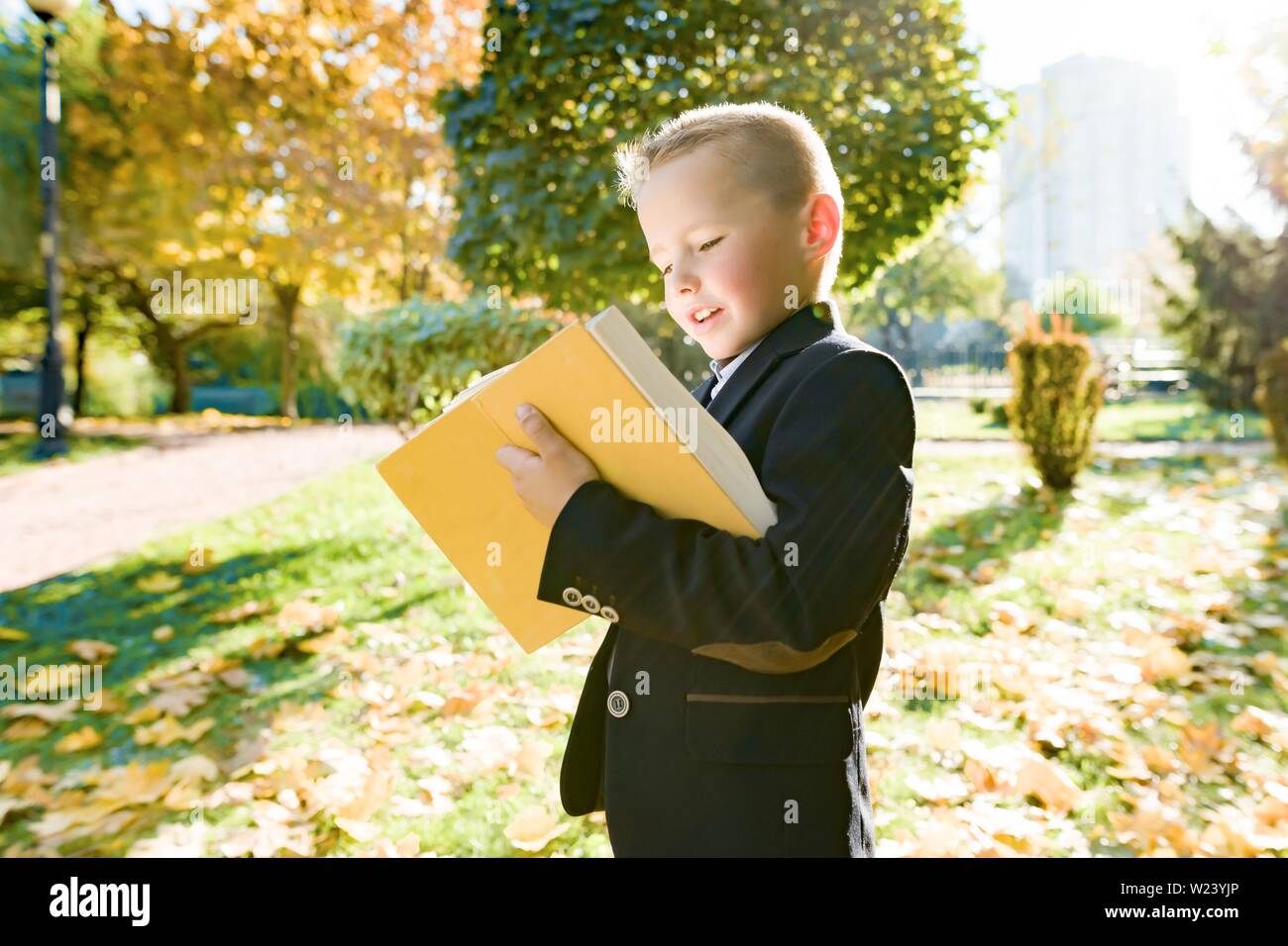 Outdoor autumn portrait of schoolboy reading book, background of yellow ...