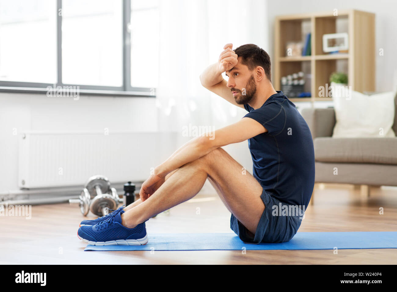 tired man sitting on exercise mat at home Stock Photo - Alamy