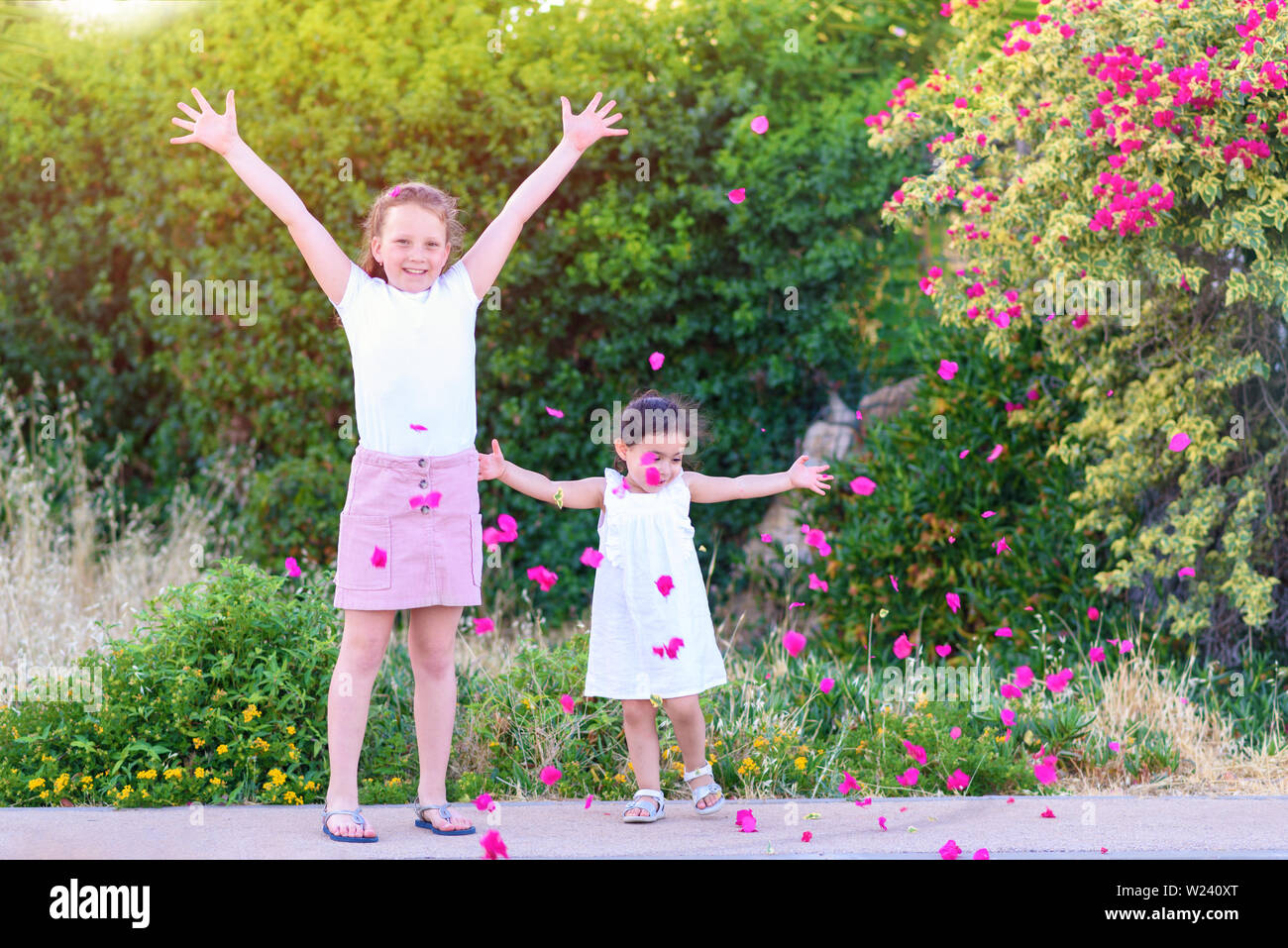 Two little girls enjoying life. Little children throw pink petals ...