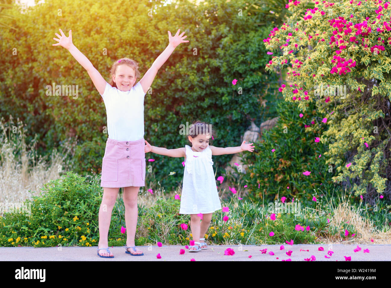 Two little girls enjoying life. Little children throw pink petals ...