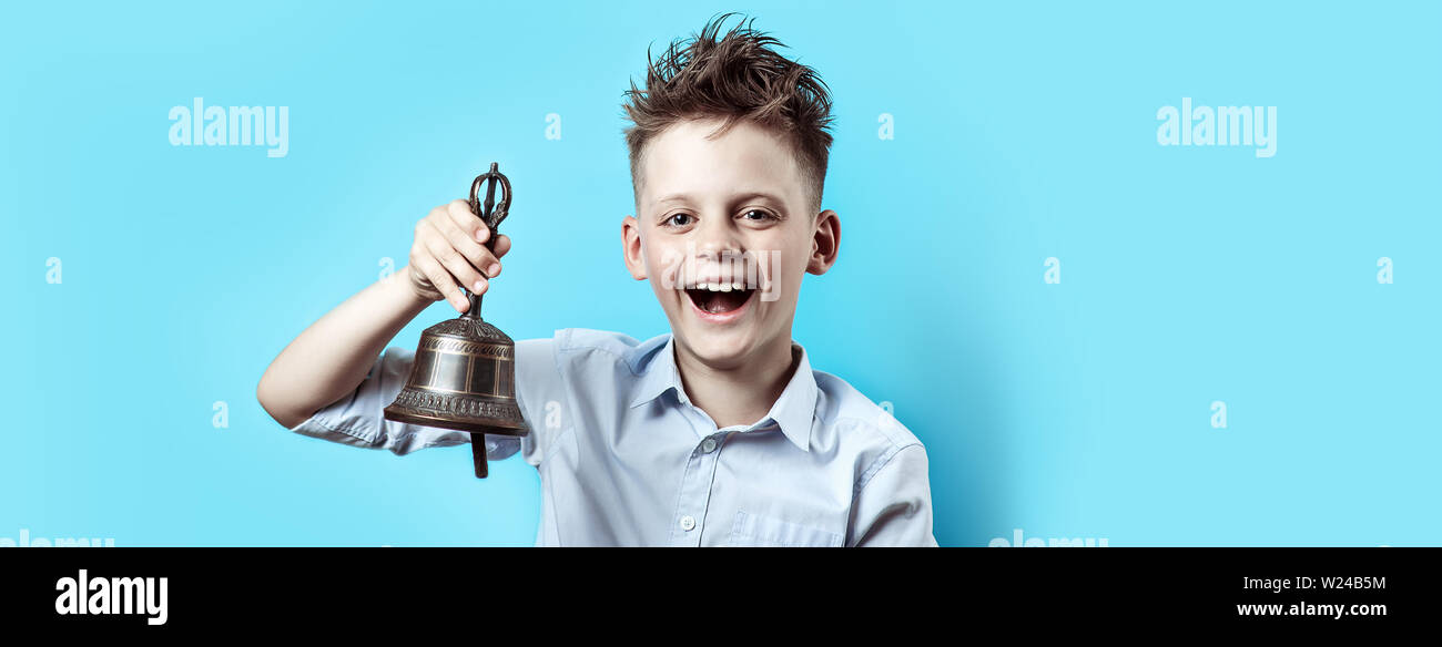 happy boy in light shirt goes to school. He has a bell in his hand ...