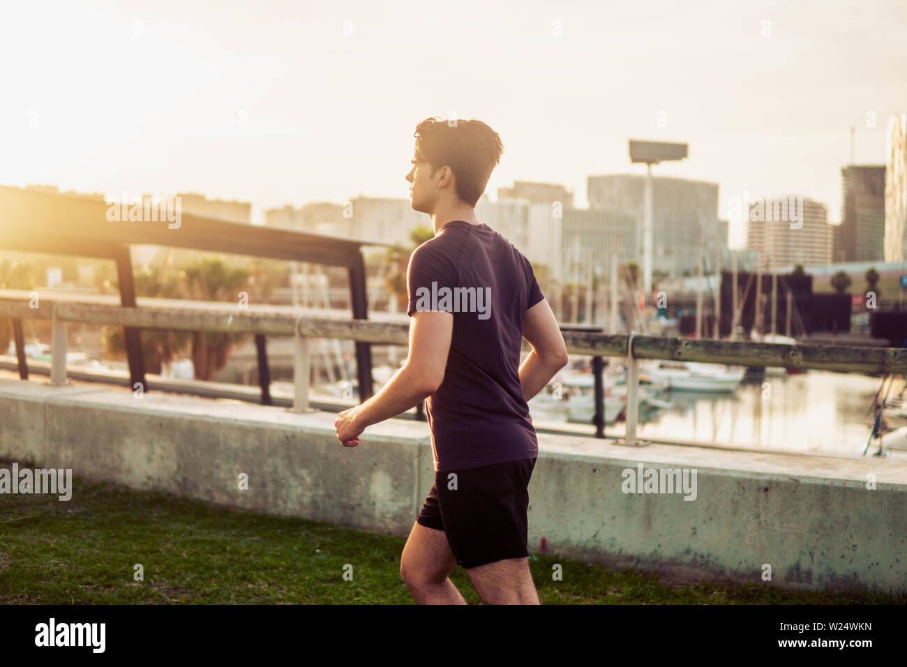 Young athletic man running at park with skyscrapers background Stock ...