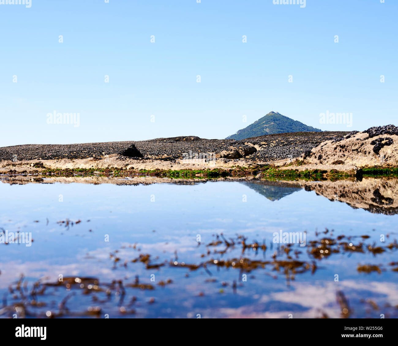 Mountain reflection on the water pond between the rocks at the beach ...