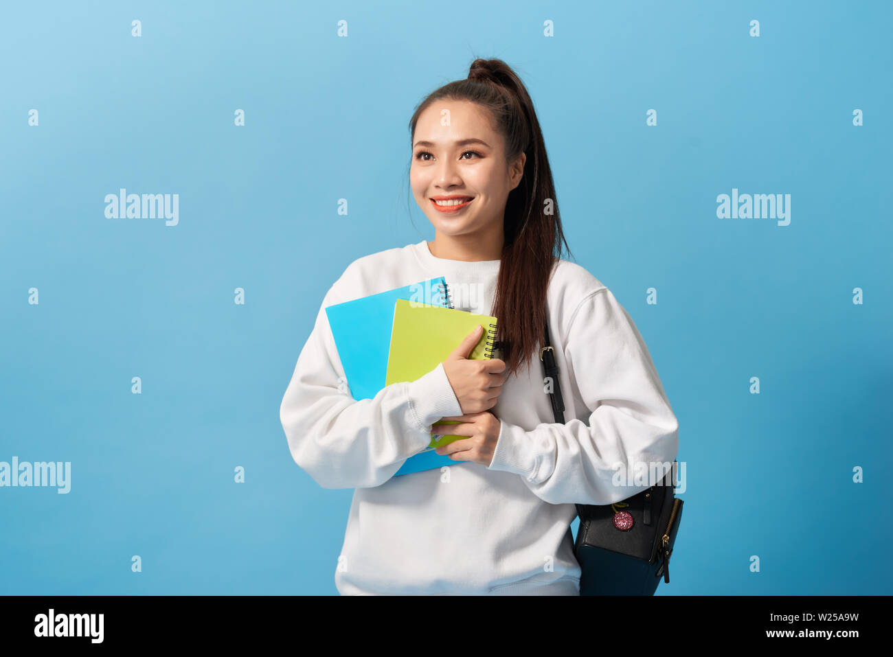 Asian student with backpack holding notebooks against light blue ...