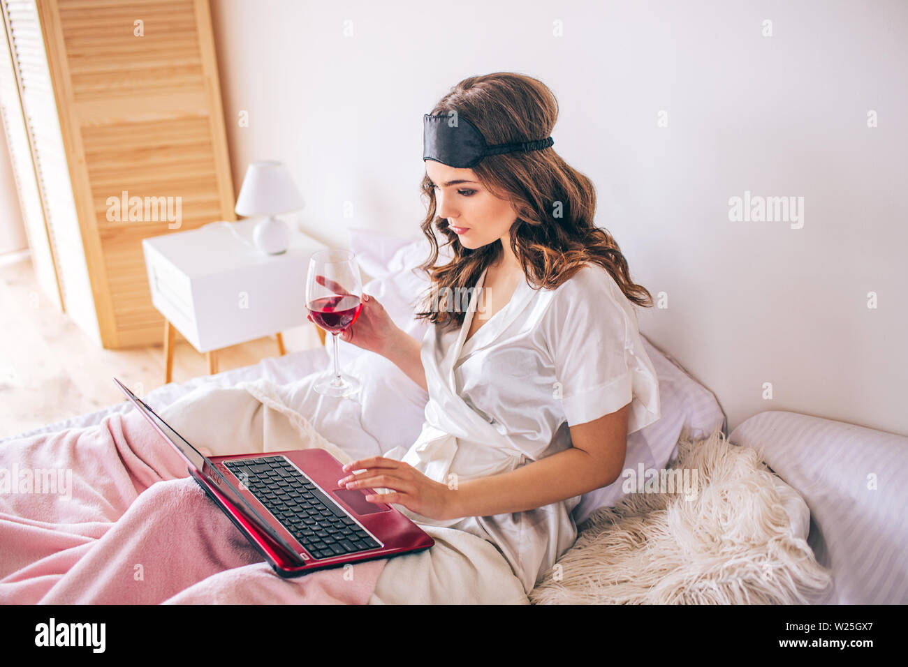 Young woman with dark hair sitting on bed in bedroom and working ...