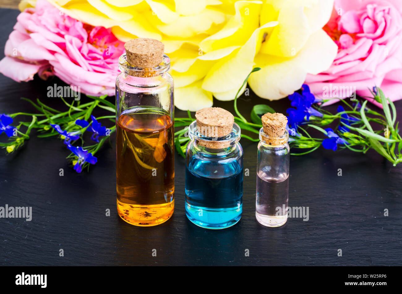 Three bottles of essential oil with fresh flowers on black background ...