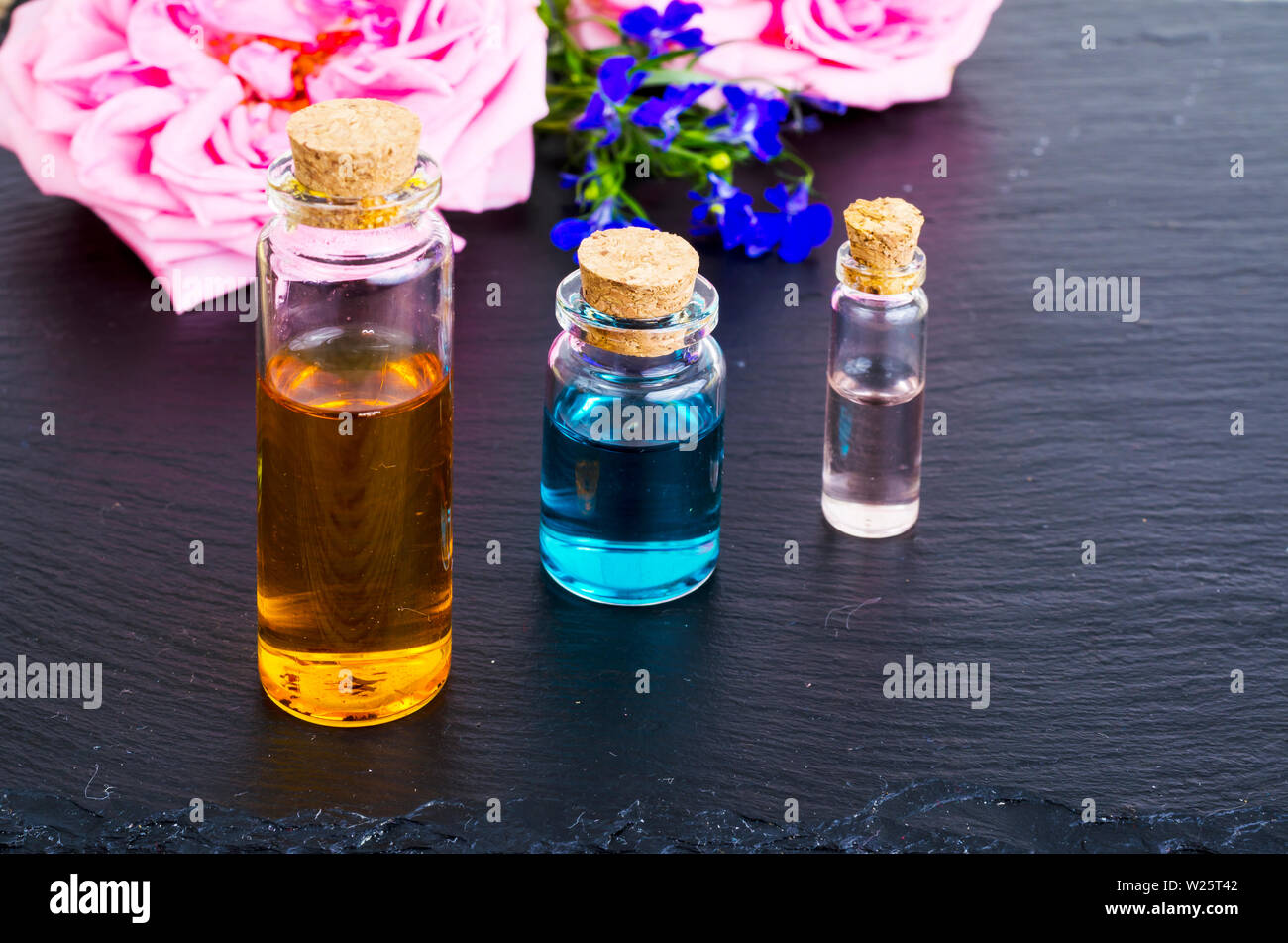 Three bottles of essential oil with fresh flowers on black background ...