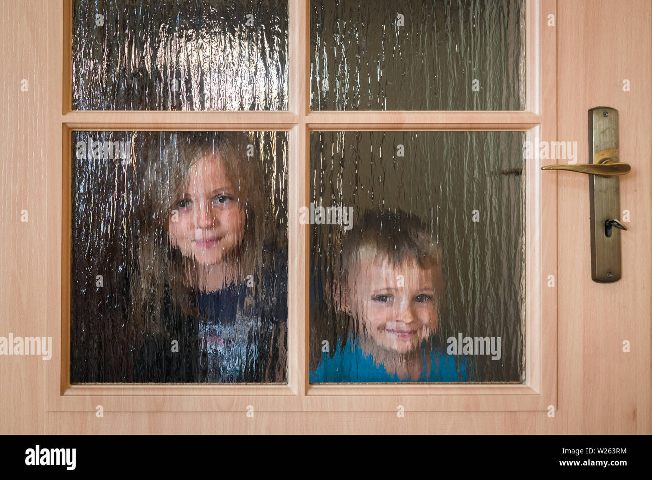 Portrait of a cute little Caucasian boy and girl hiding behind a door ...