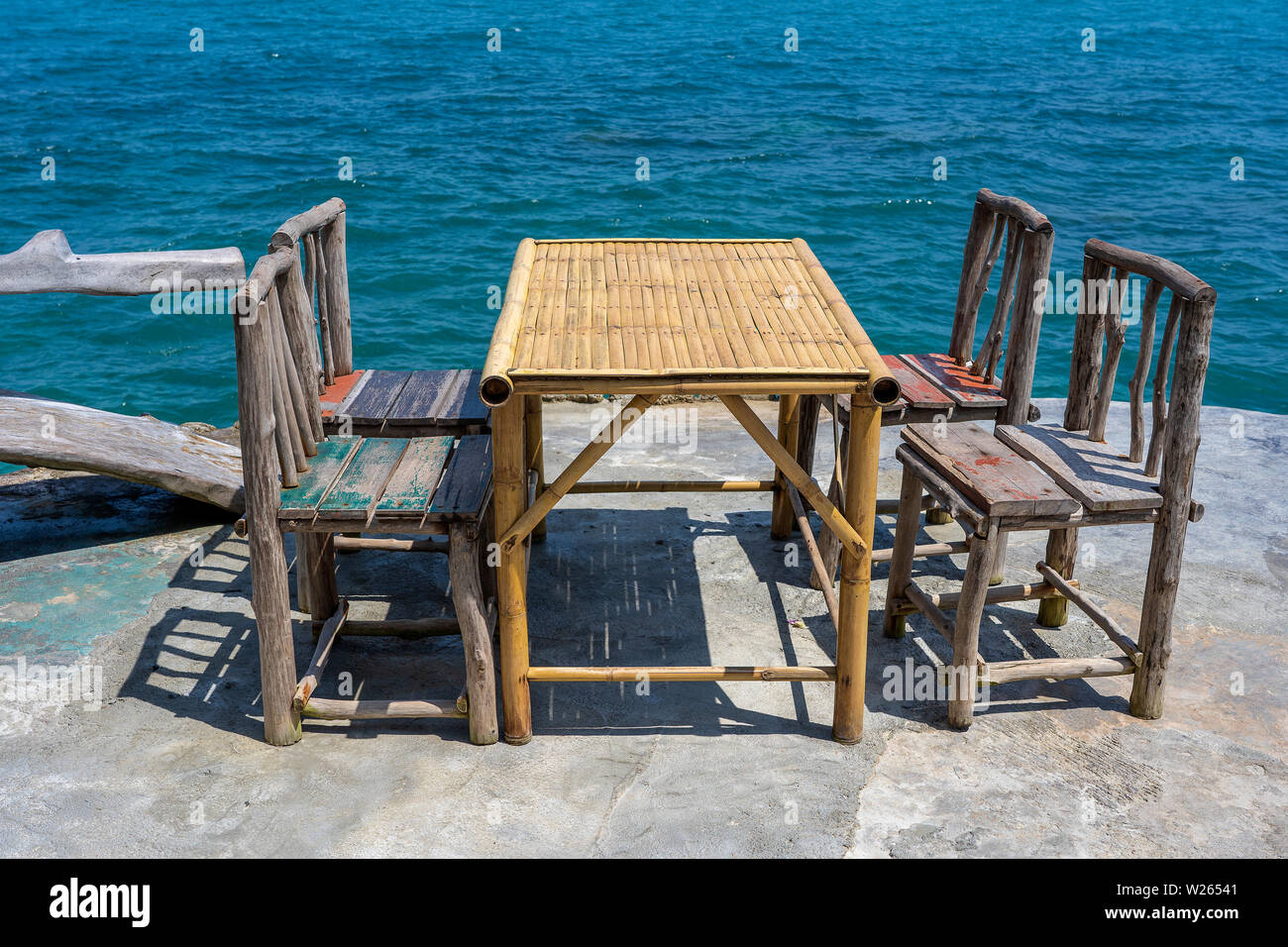 Bamboo table and wooden chairs in empty cafe next to sea water in tropical beach. Close up ...