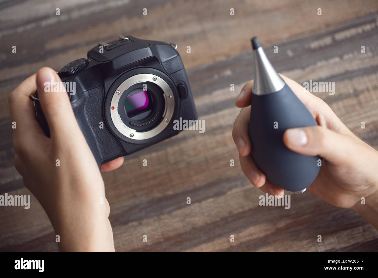 Two hands cleaning digital camera sensor from dust with air blower ...
