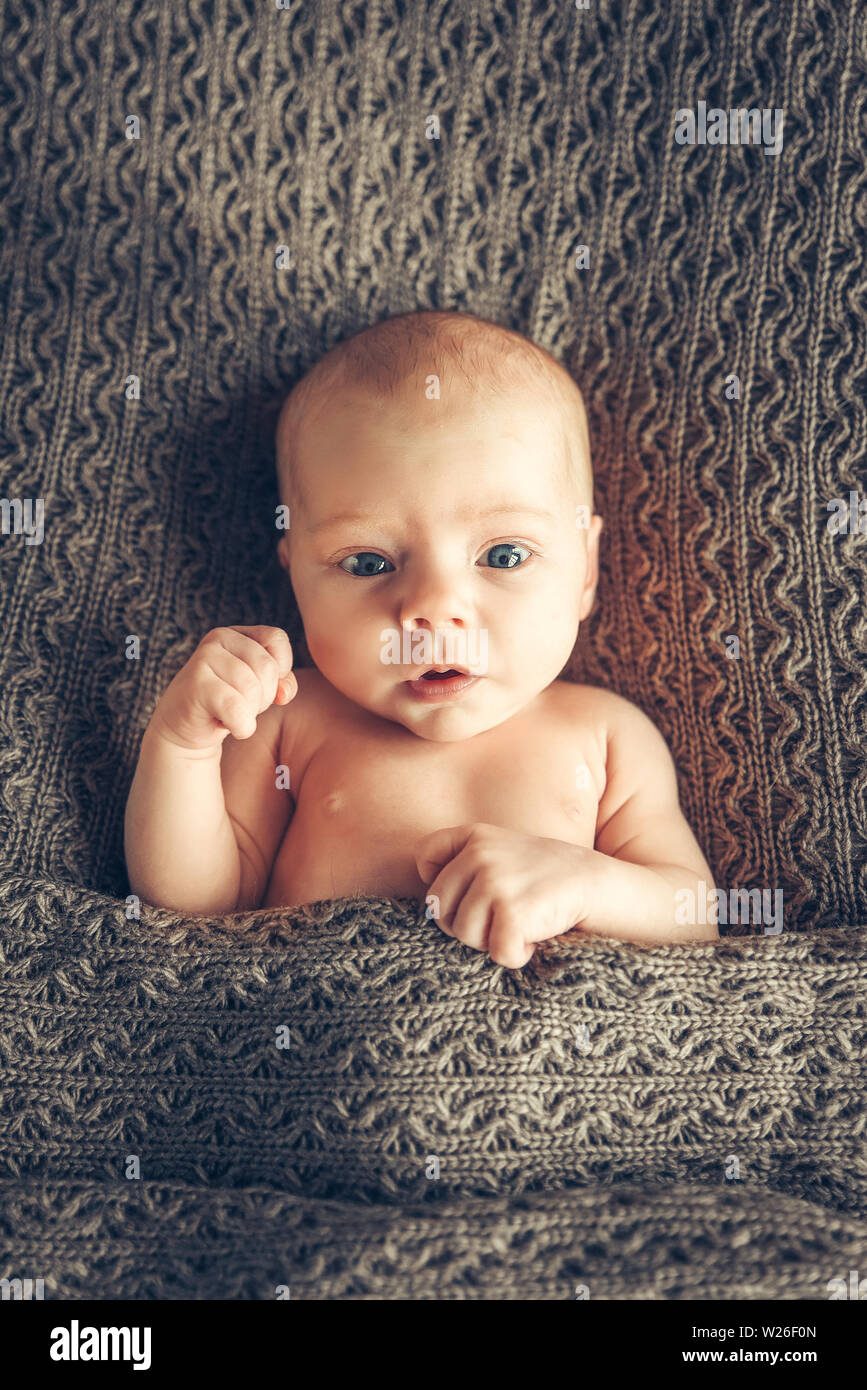 Funny portrait of a full face baby lying in a crib, hand raised up ...