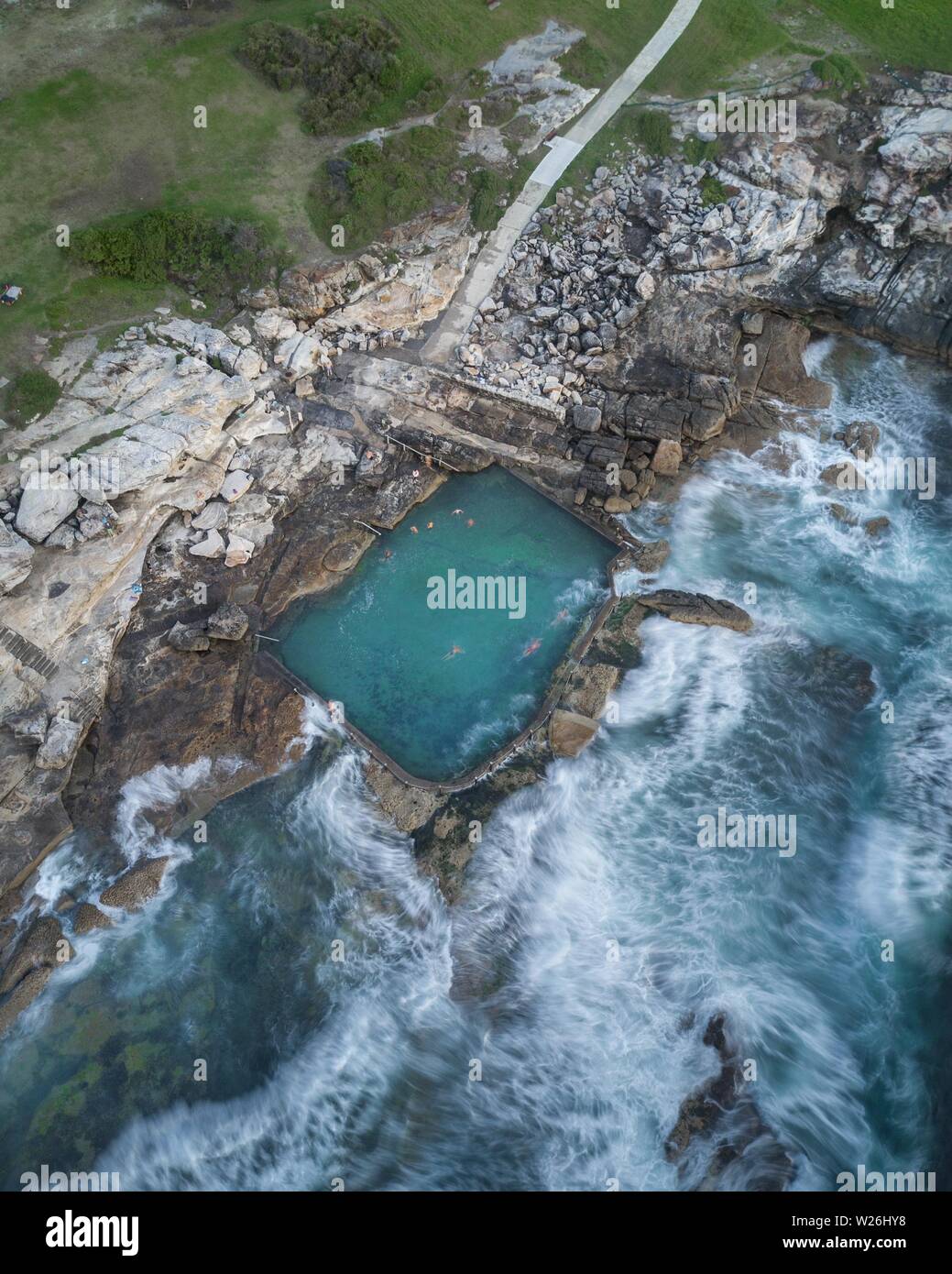 Aerial shot of people swimming in a large pool built on the rocky coast ...