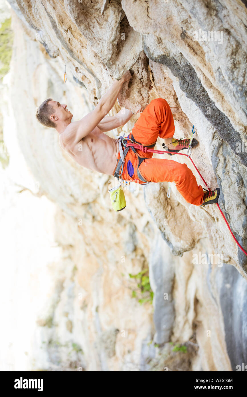 Caucasian young man climbing challenging route on overhanging cliff ...