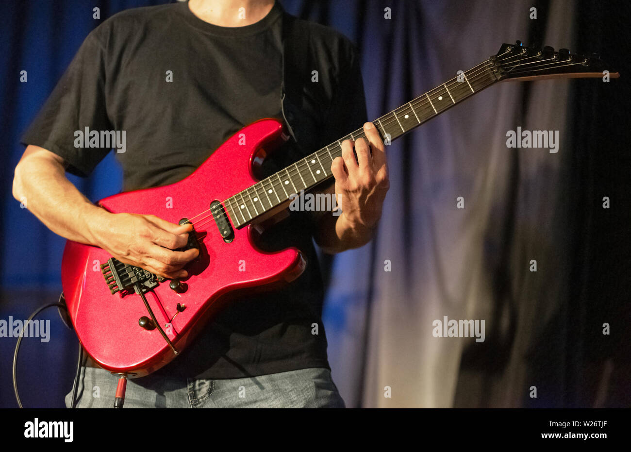 Musician playing red electric guitar on stage Stock Photo - Alamy