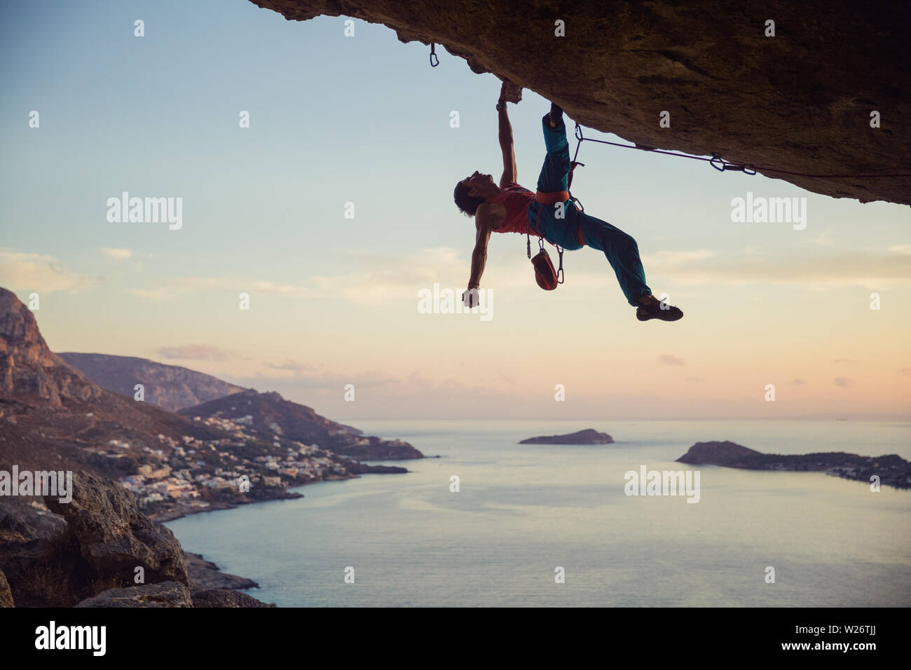 Young man struggling to climb ledge on cliff, view of coast below Stock ...