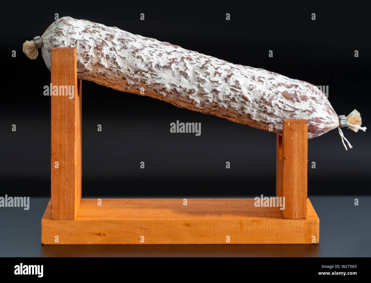 Whole spicy salami displayed on a wooden stand over a dark background ...