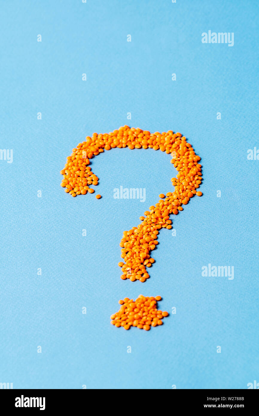 Flat lay question mark made from small orange lentils over blue ...