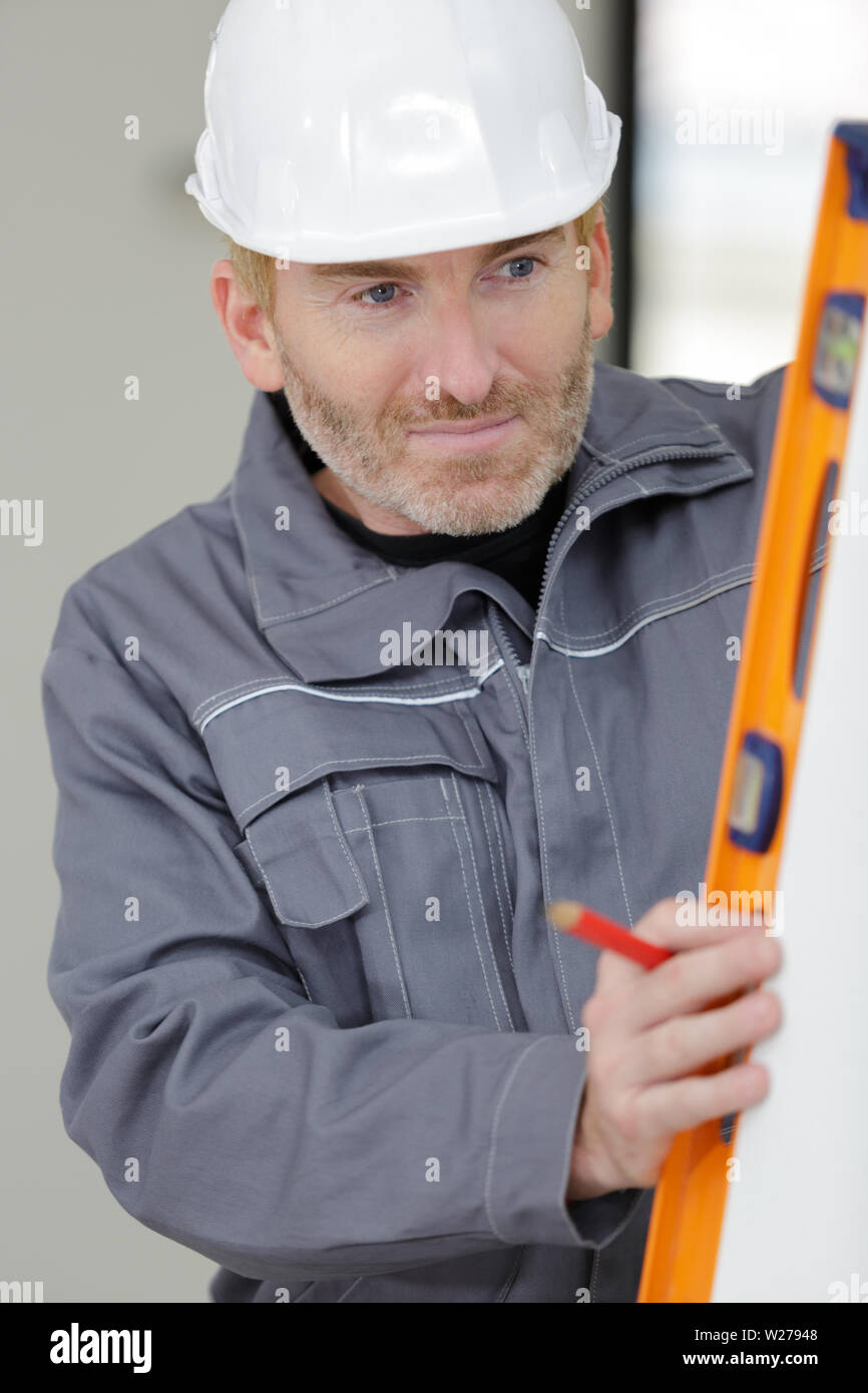 repairman in helmet is measuring wall with level Stock Photo - Alamy