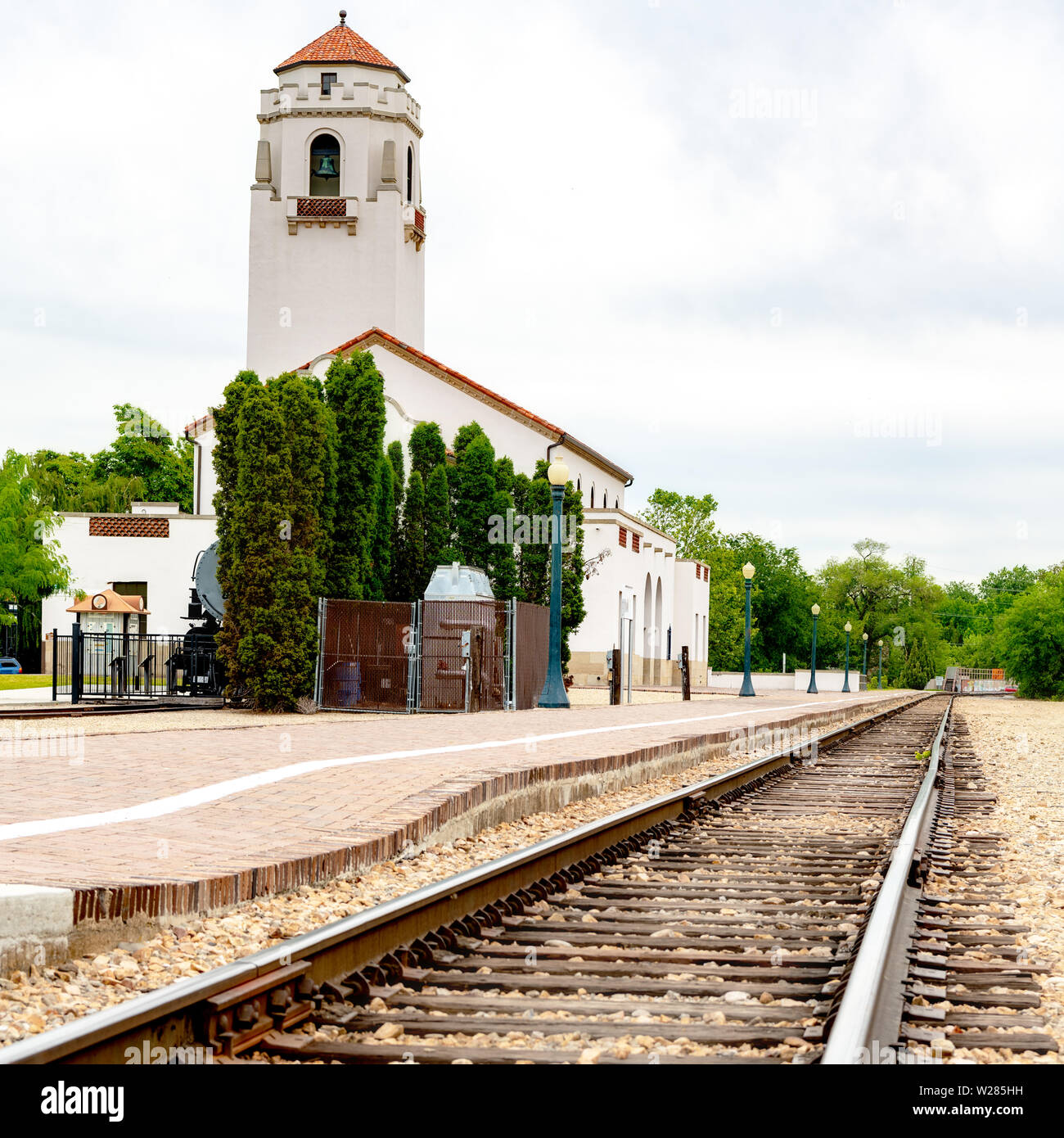 Train tracks pass a depot with brick walkway and trees Stock Photo - Alamy
