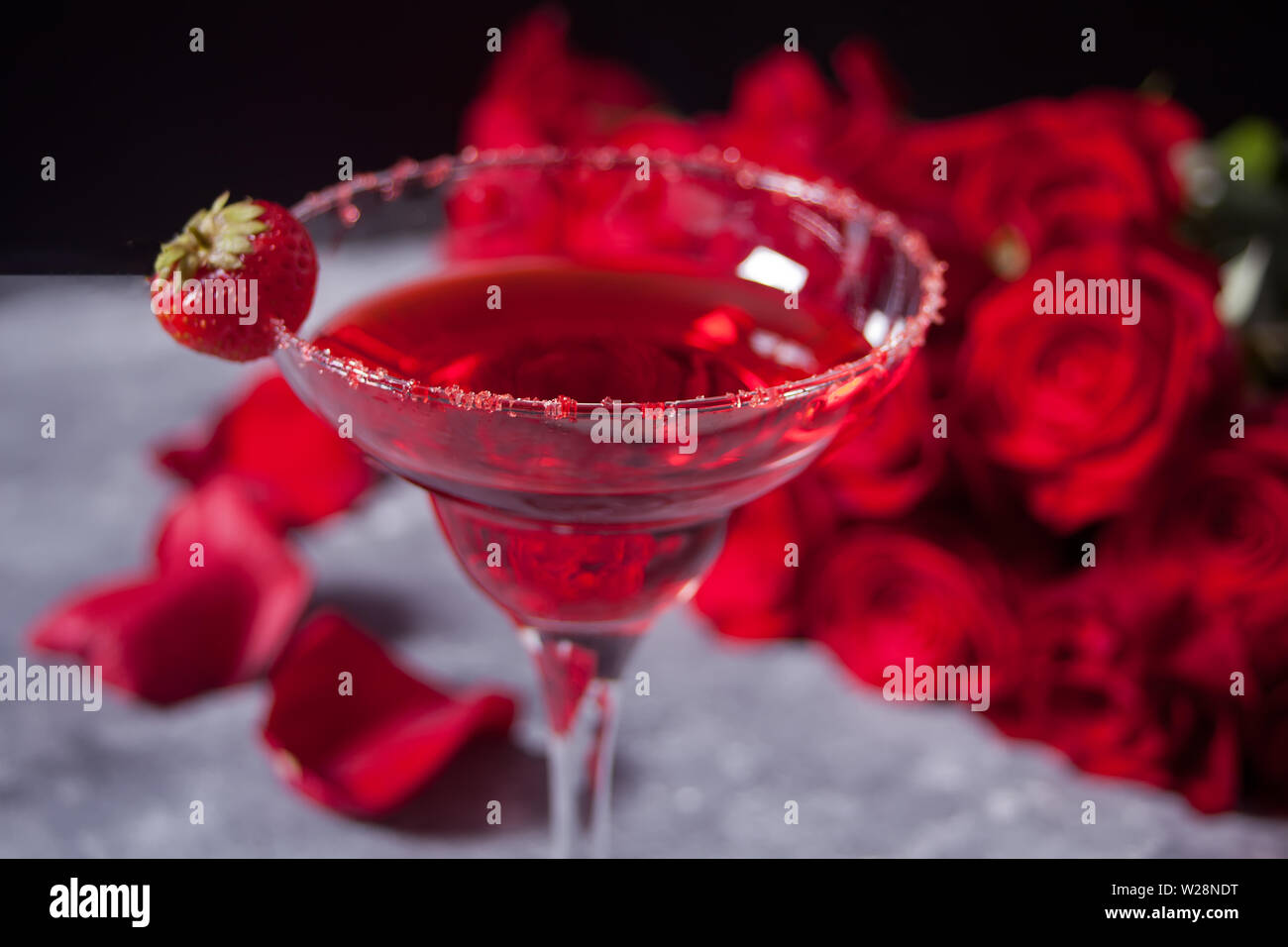 Red fresh exotic alcoholic cocktail in clear glass and red roses on the ...