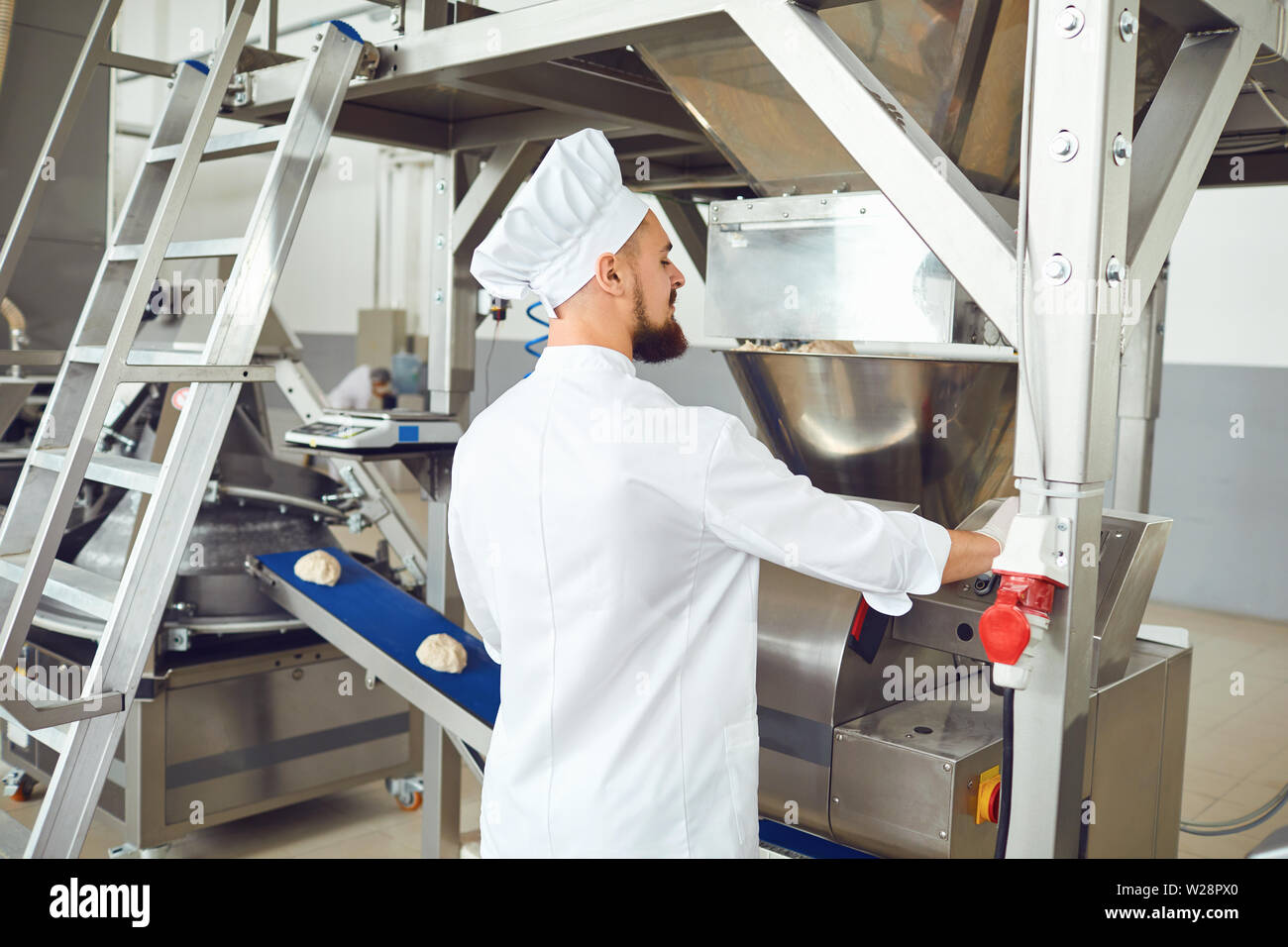 A baker in white uniform controls the process of creating dough for ...