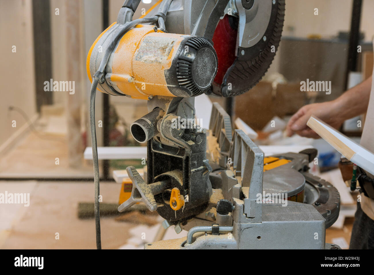 Finishing work the worker cuts wood moldings baseboard on the miter saw ...