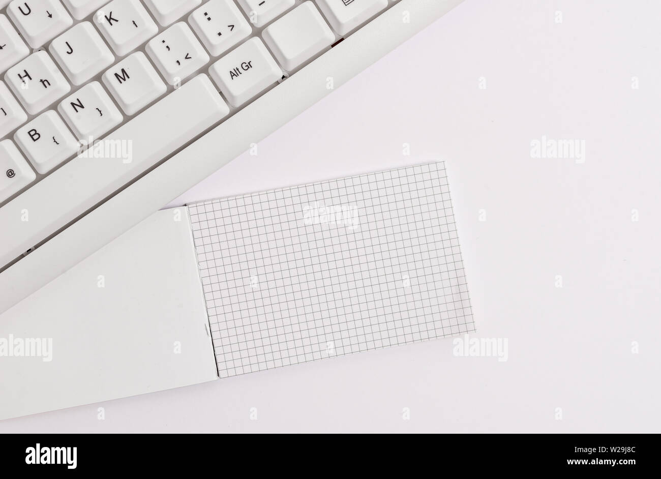 White pc keyboard with empty note paper above white background ...