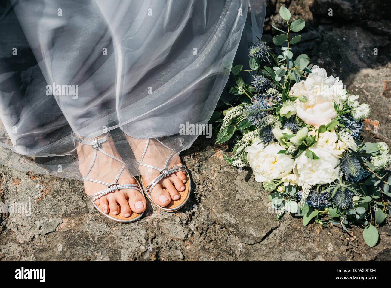 The legs of the bride are in a dress and the wedding bridal bouquet is ...