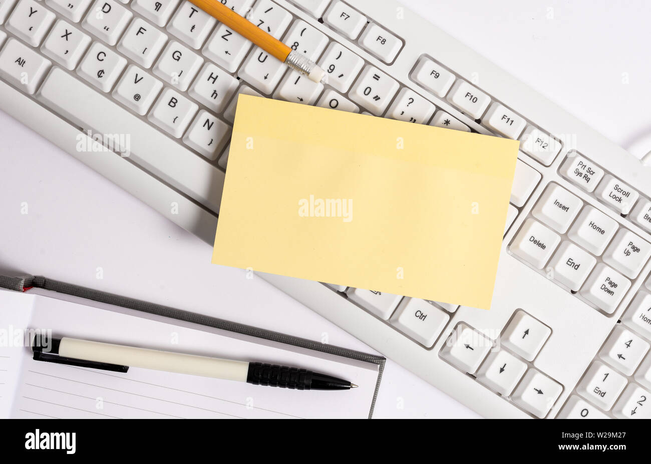 White pc keyboard with empty note paper and paper clips above white ...