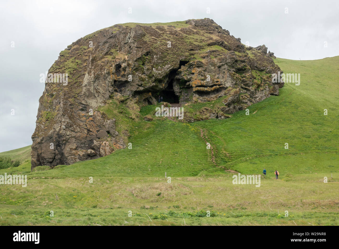 Visitors walking up to Loftsalahellir Cave, a tuff rock on the ...