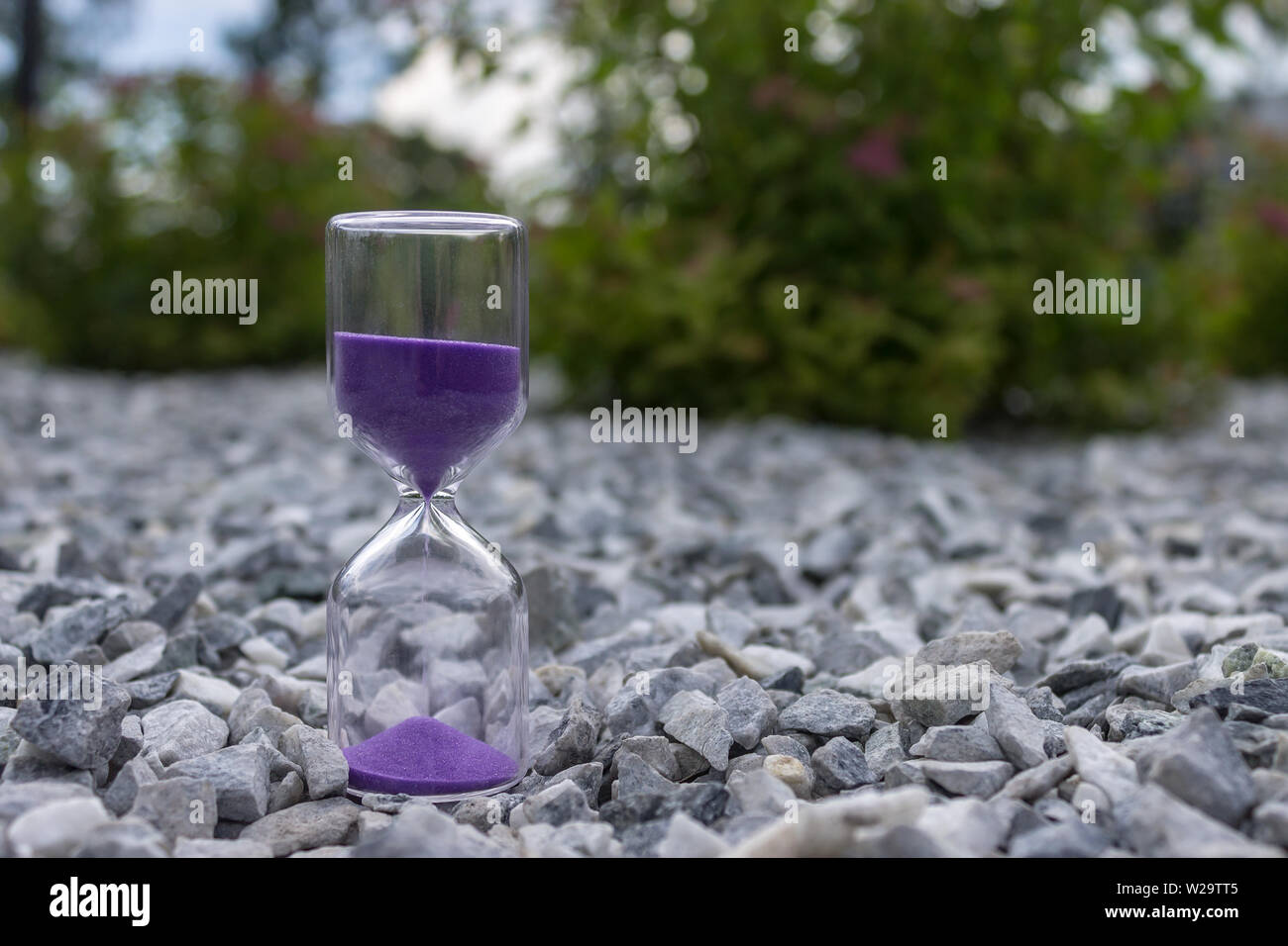 Hourglass on stones in a public park on the background of green bushes ...