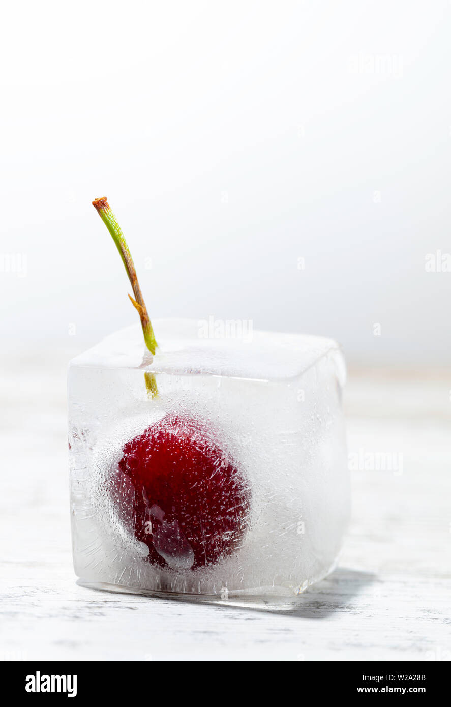 ice cube with a frozen cherry inside on a wooden table and white ...