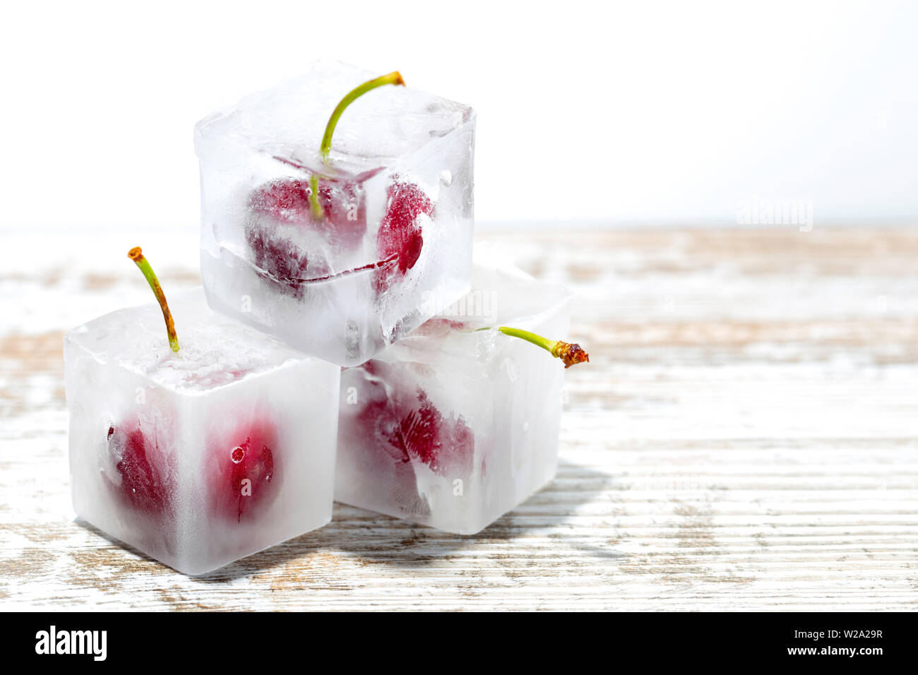 ice cubes with cherries inside on a wooden table and white background ...