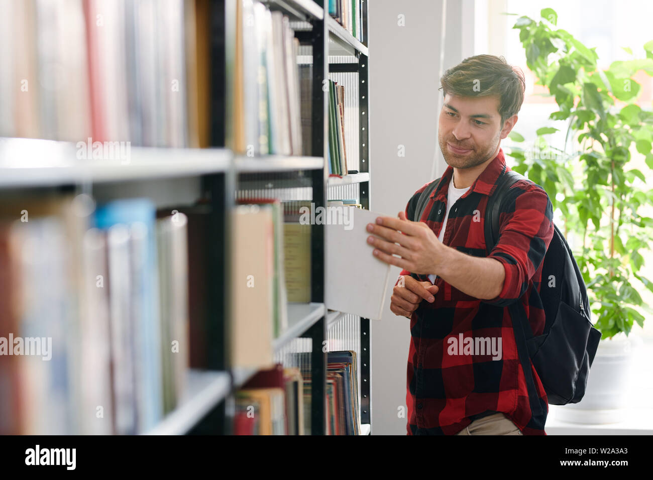 College student with backpack looking through books in college library ...