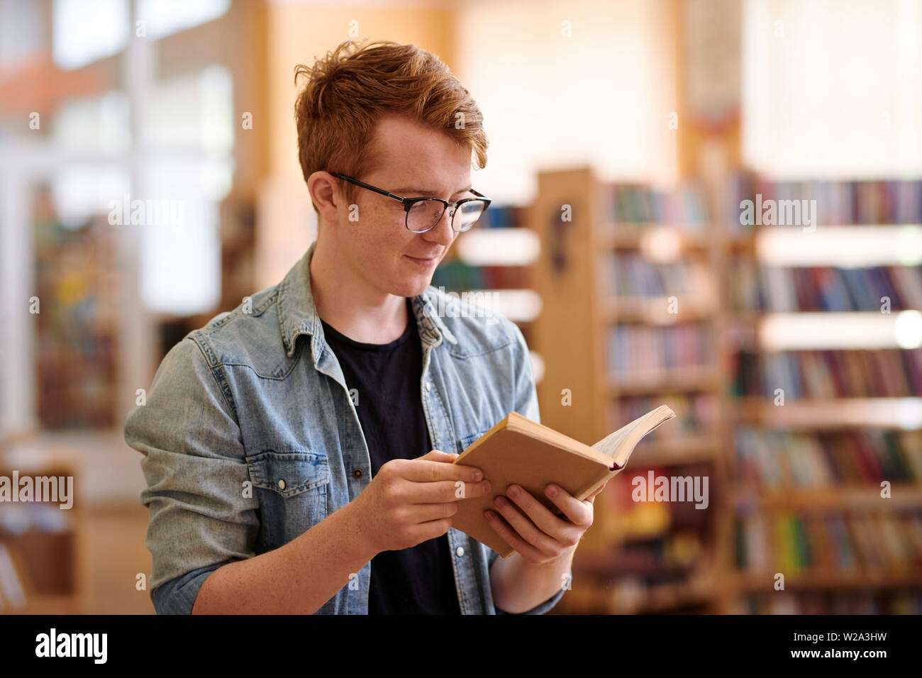 Young college student in denim shirt and black tee reading book Stock ...
