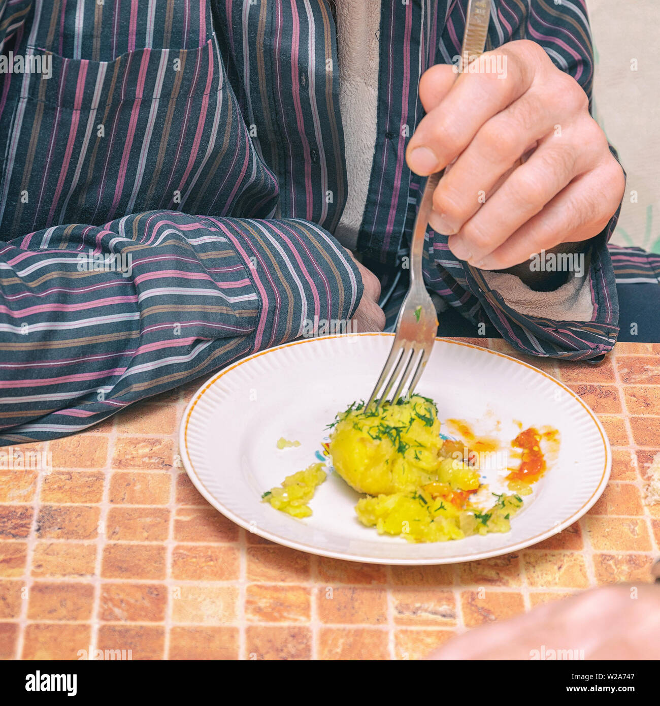 Man at the table in the kitchen eating potatoes Stock Photo - Alamy