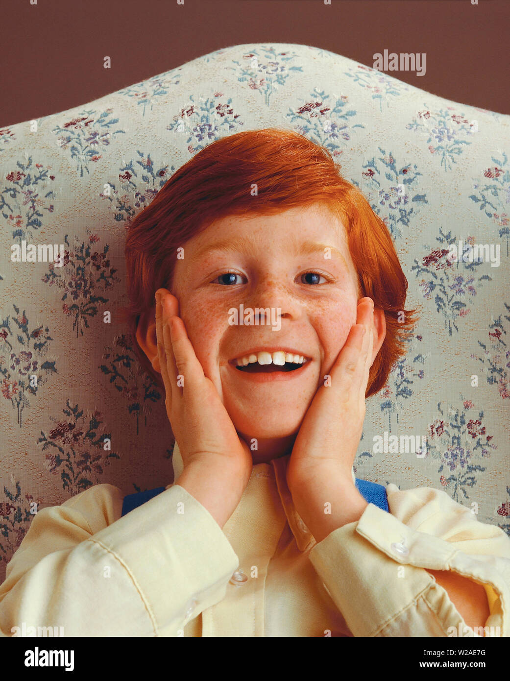 Young boy sitting in a chair with his hands on his cheeks with a big ...
