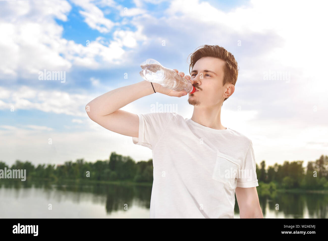 young guy drinks fresh water against of the lake and the forest ...