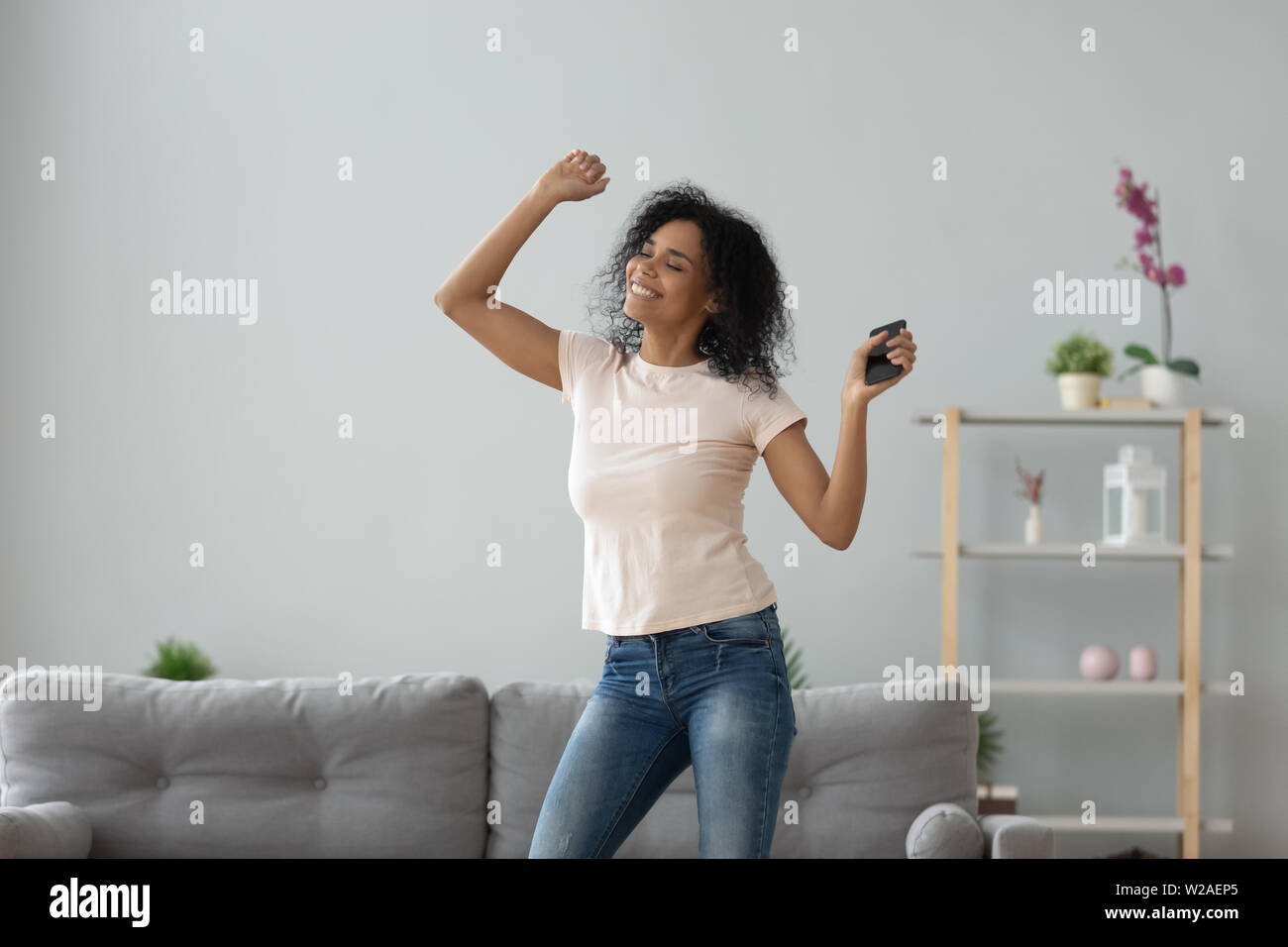 Smiling active black woman dancing alone holding phone at home Stock ...