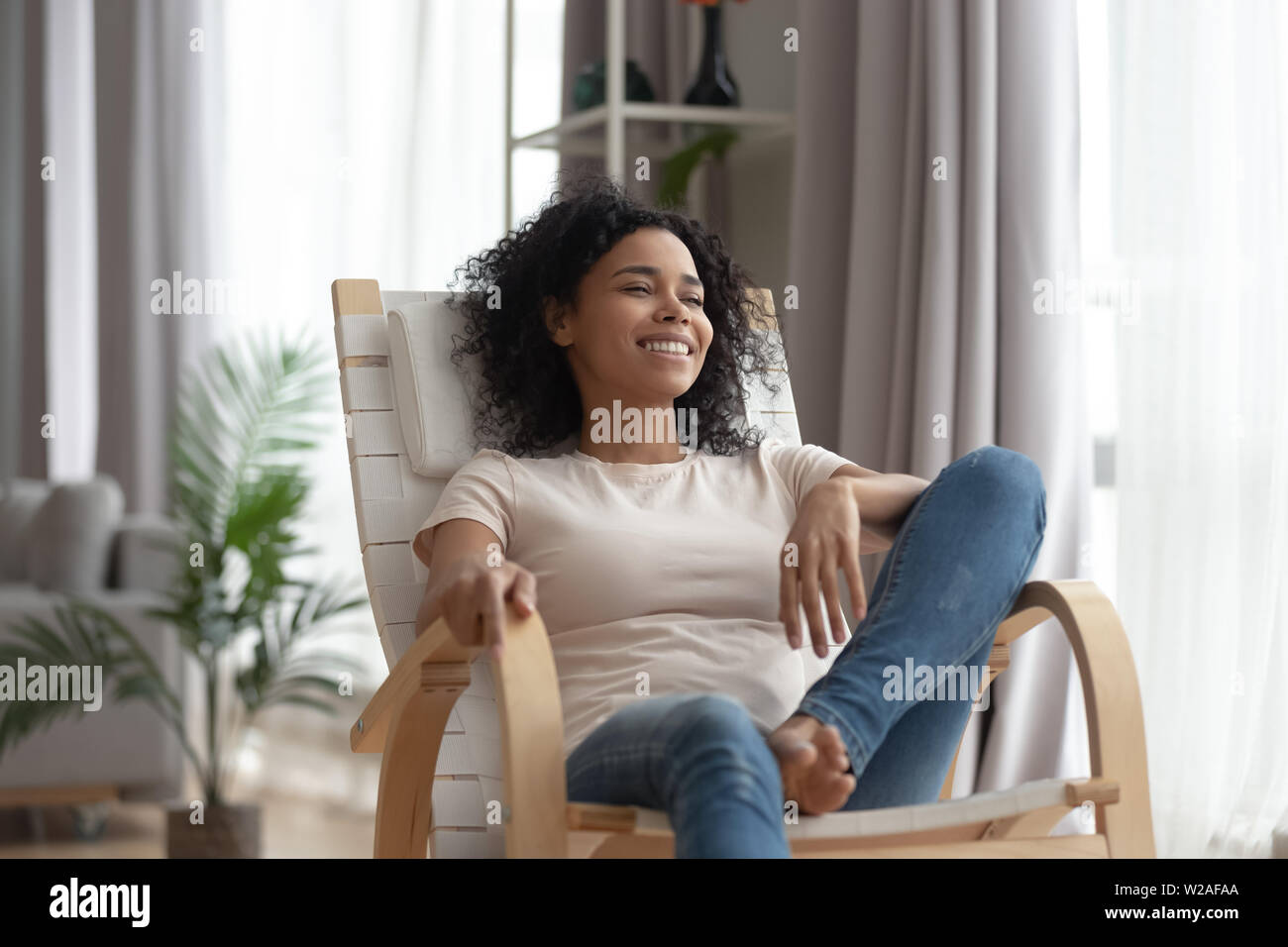 Smiling calm black woman relaxing in comfortable wooden rocking chair ...