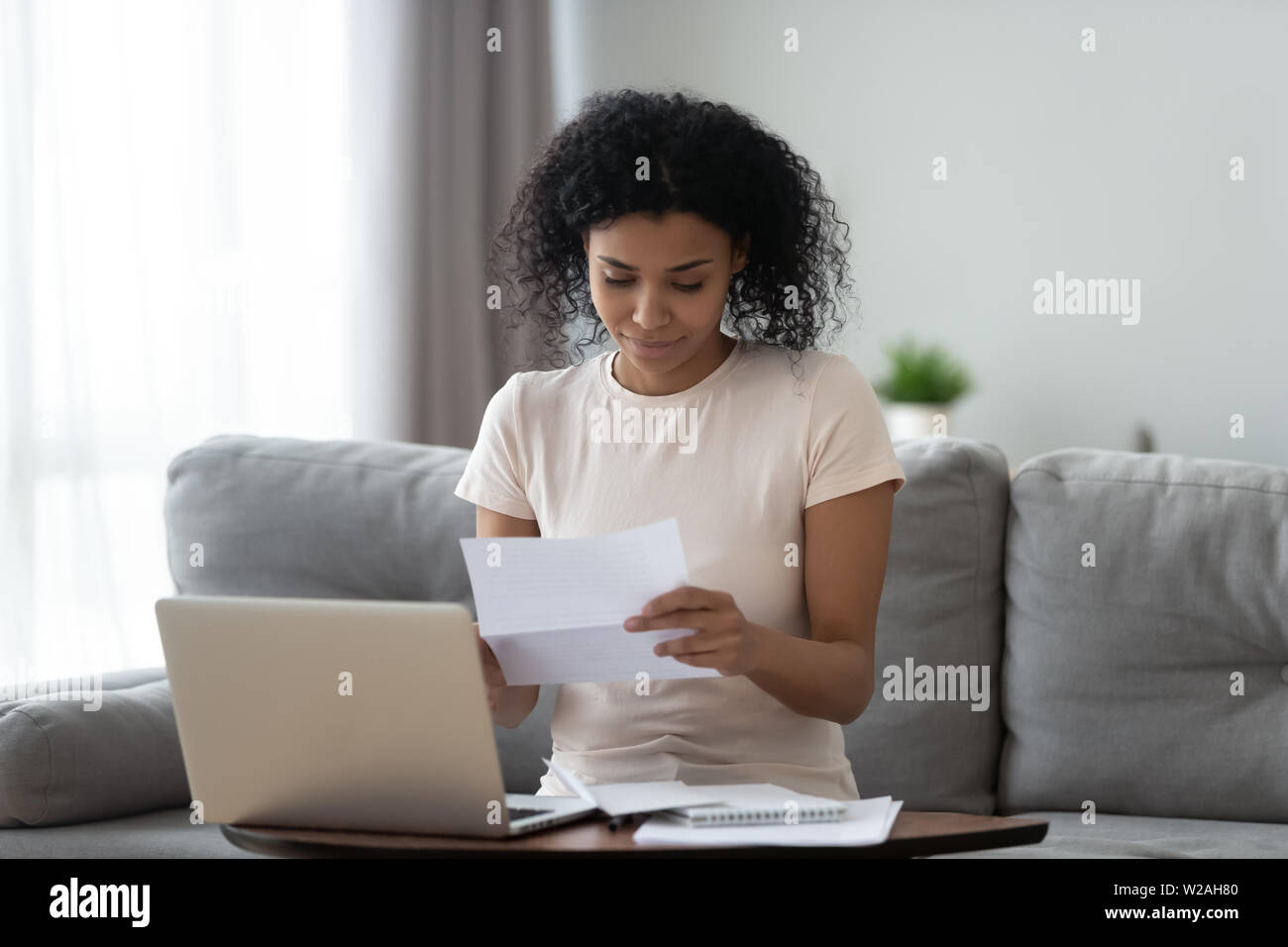 Smiling african girl student reading paper letter sit on sofa Stock ...