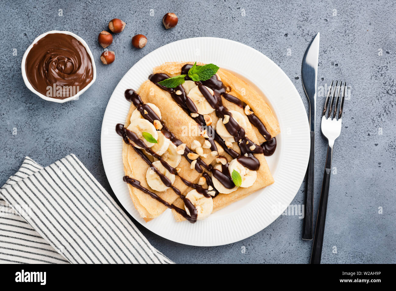 Crepe with banana, chopped nuts and chocolate sauce on white plate ...
