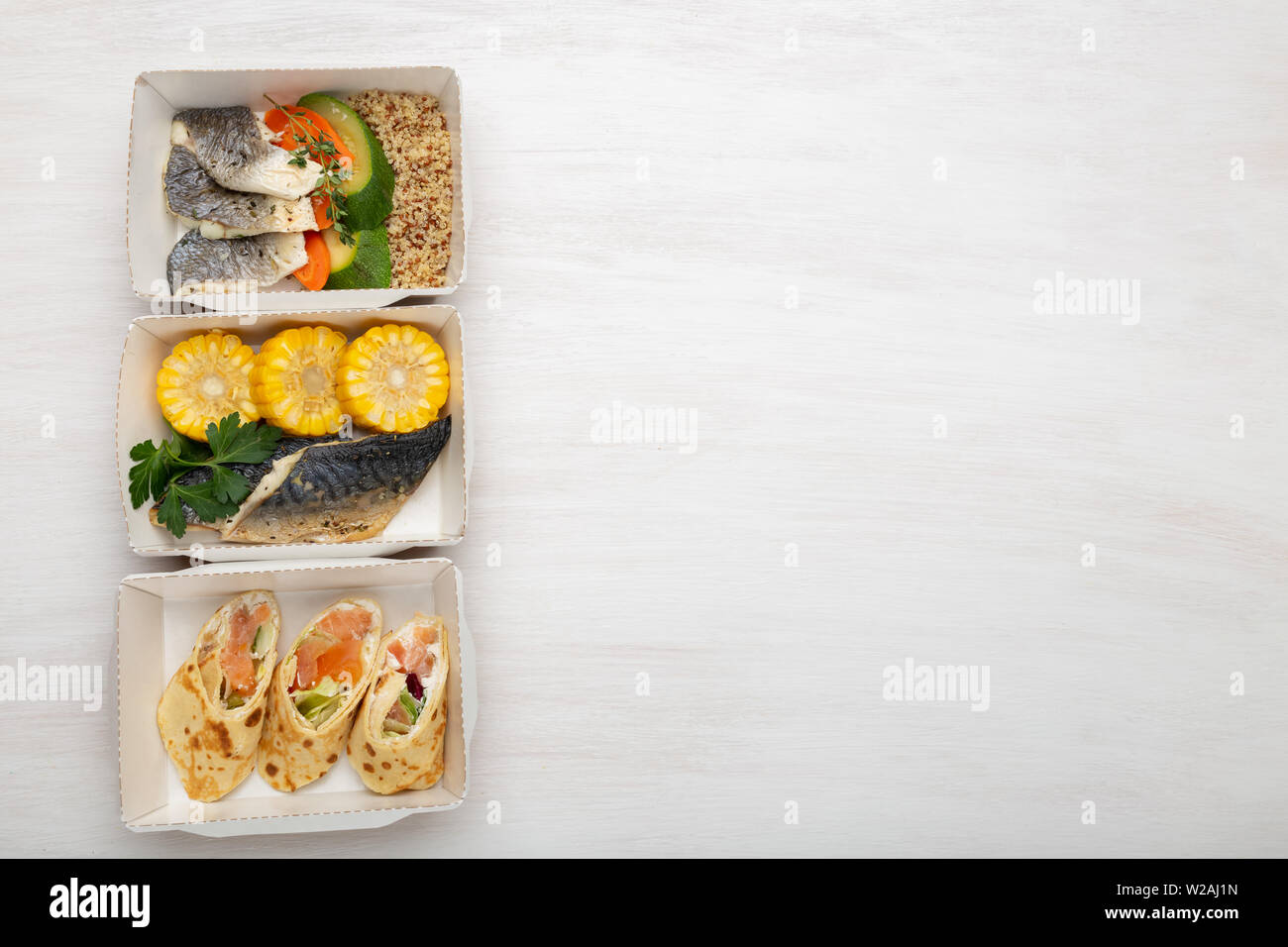 Three kinds of lunch boxes with fish and vegetables lie on a white ...