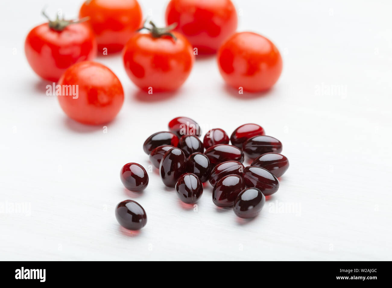 Tomatoes lie on a white table next to vitamins in the form of jelly on ...