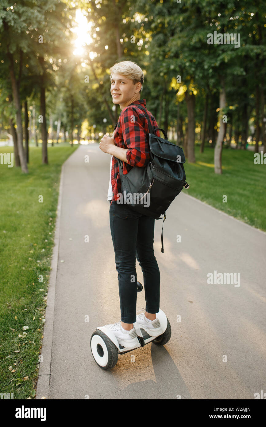 Young man with backpack riding on mini gyro board in summer park ...